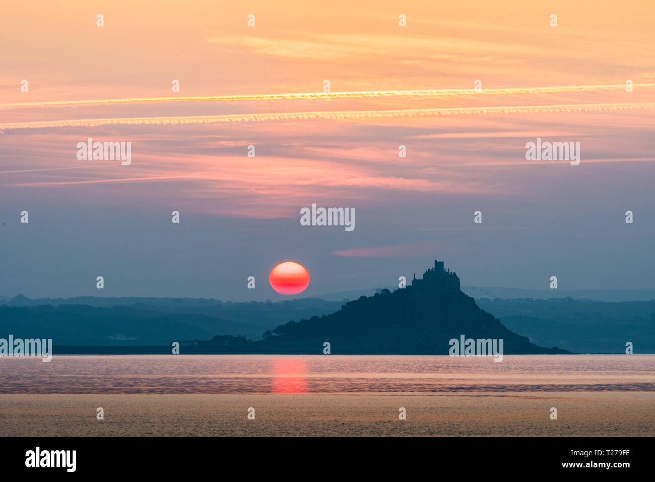 Red sun rising beside St Michaels Mount Cornwall reflecting in the sea ...
