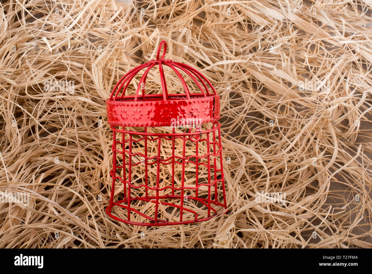 Red color bird cage placed on a straw background Stock Photo - Alamy