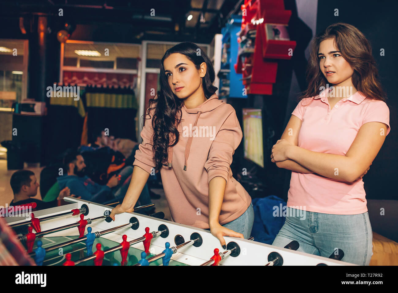 Serious and upset young women stand together at table soccer. They look ...