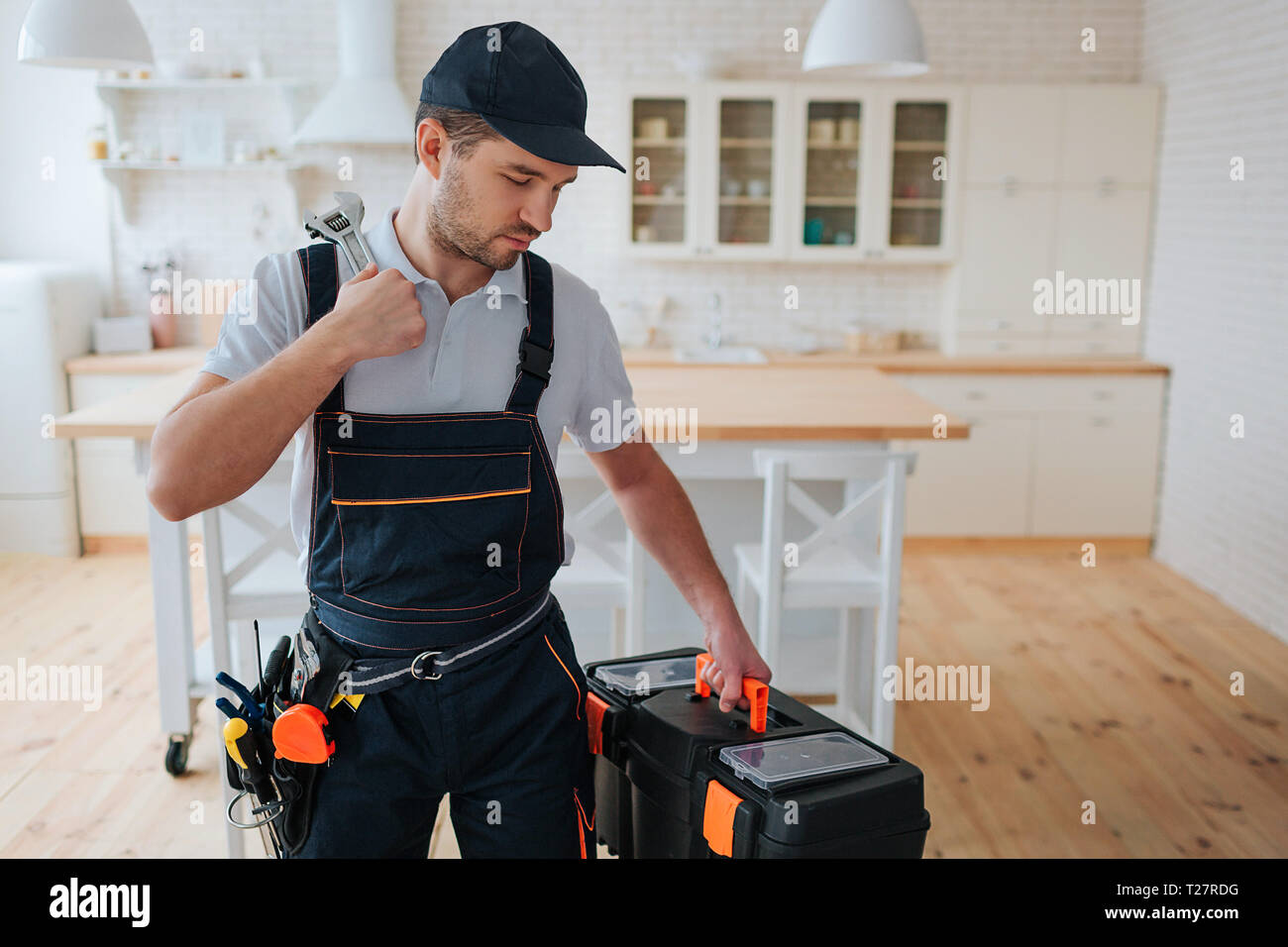 Serious young man stand in kitchen and look at tool box in his hand ...