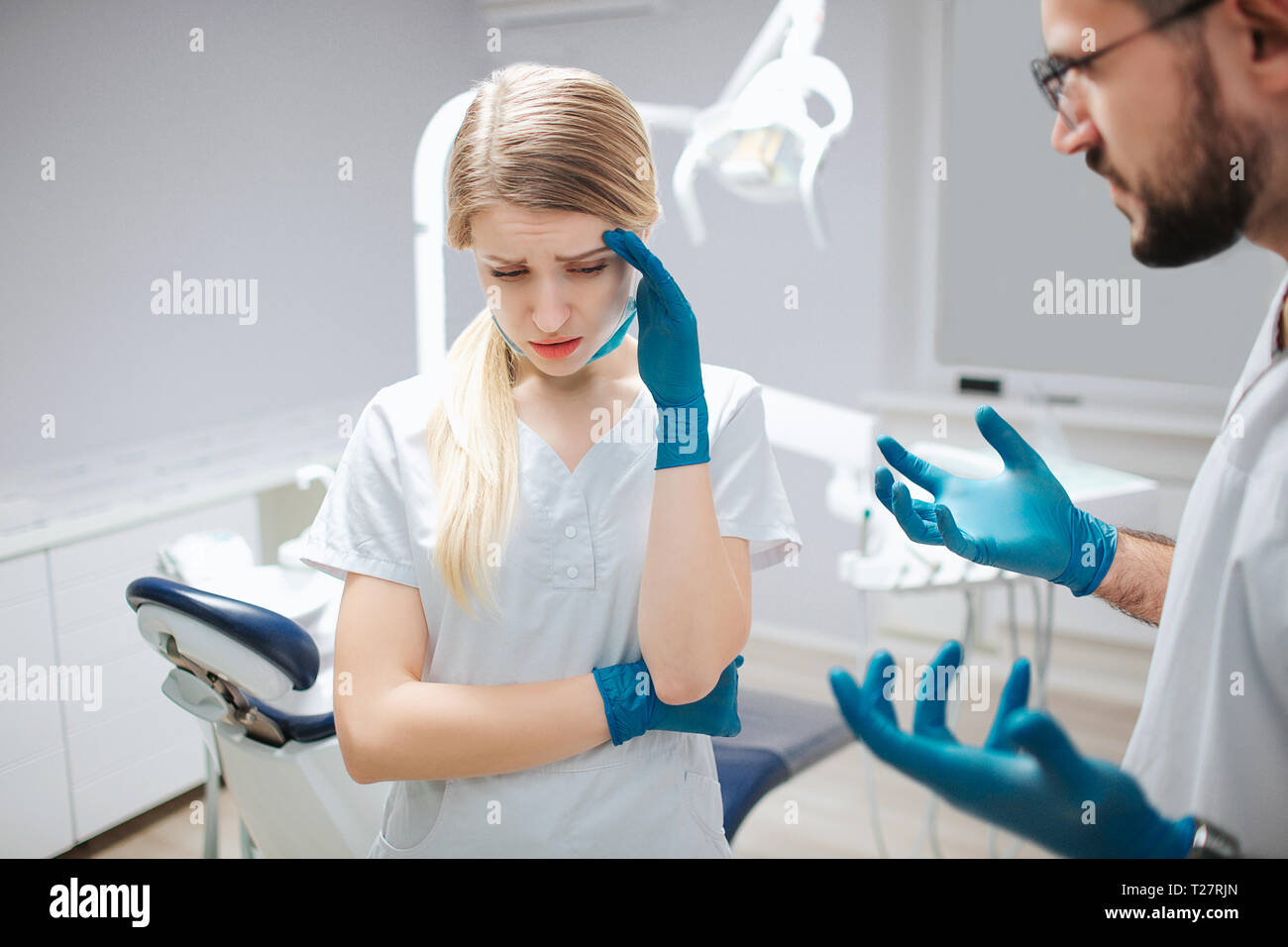 Young woman in white robe stand in room with dentist. She hold hand on ...