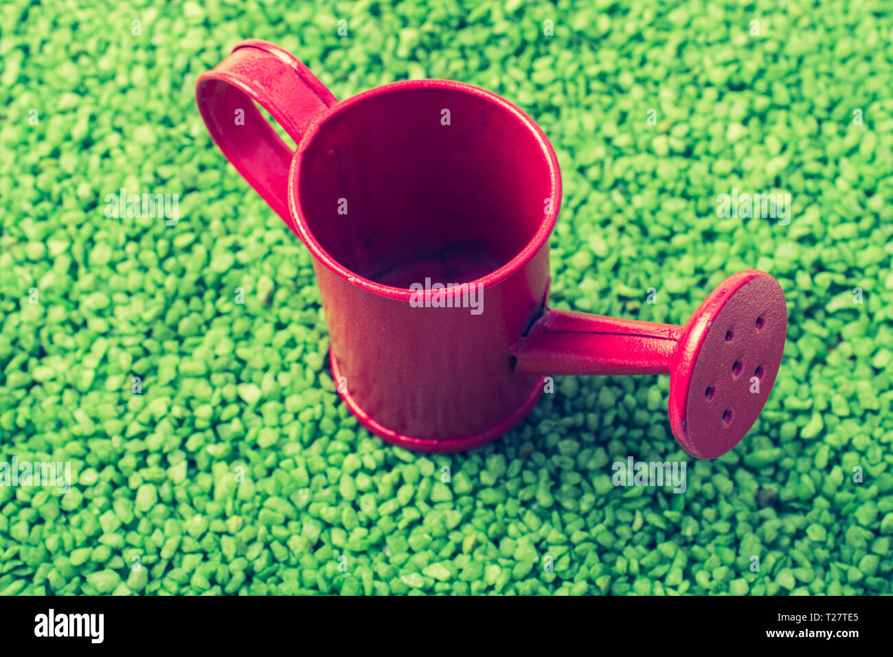 Little red color watering can on green sand Stock Photo - Alamy