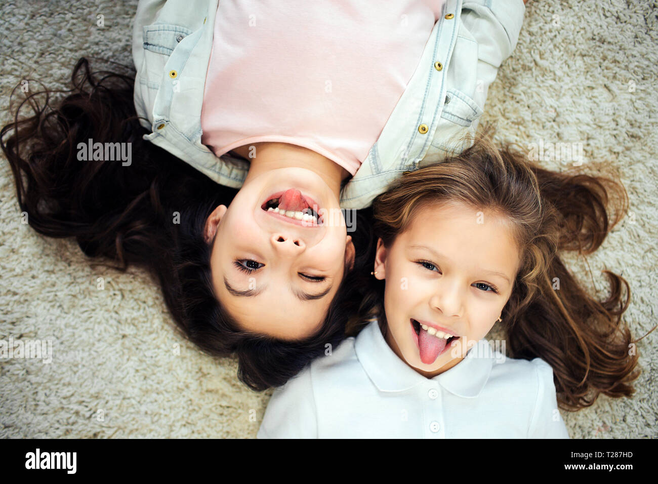 Cheerful teenagers have fun. They lying on carpet head to head and show ...