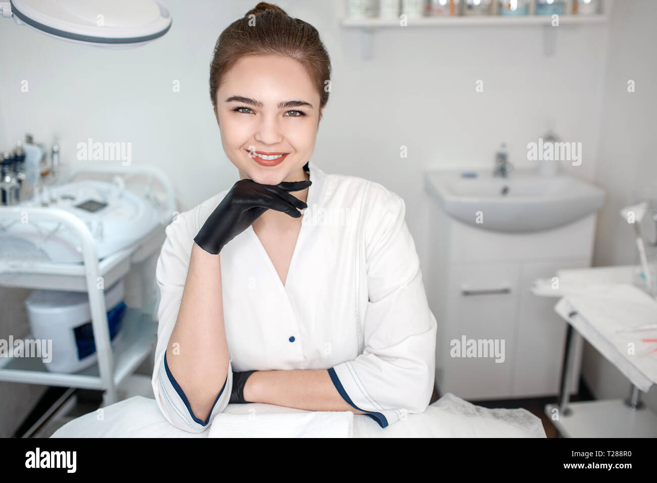 Positive nice young beautician sit in room and pose on camera. She ...