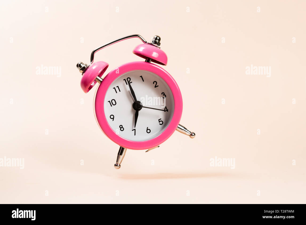The morning alarm clock jumping up from the bell on a peach background ...