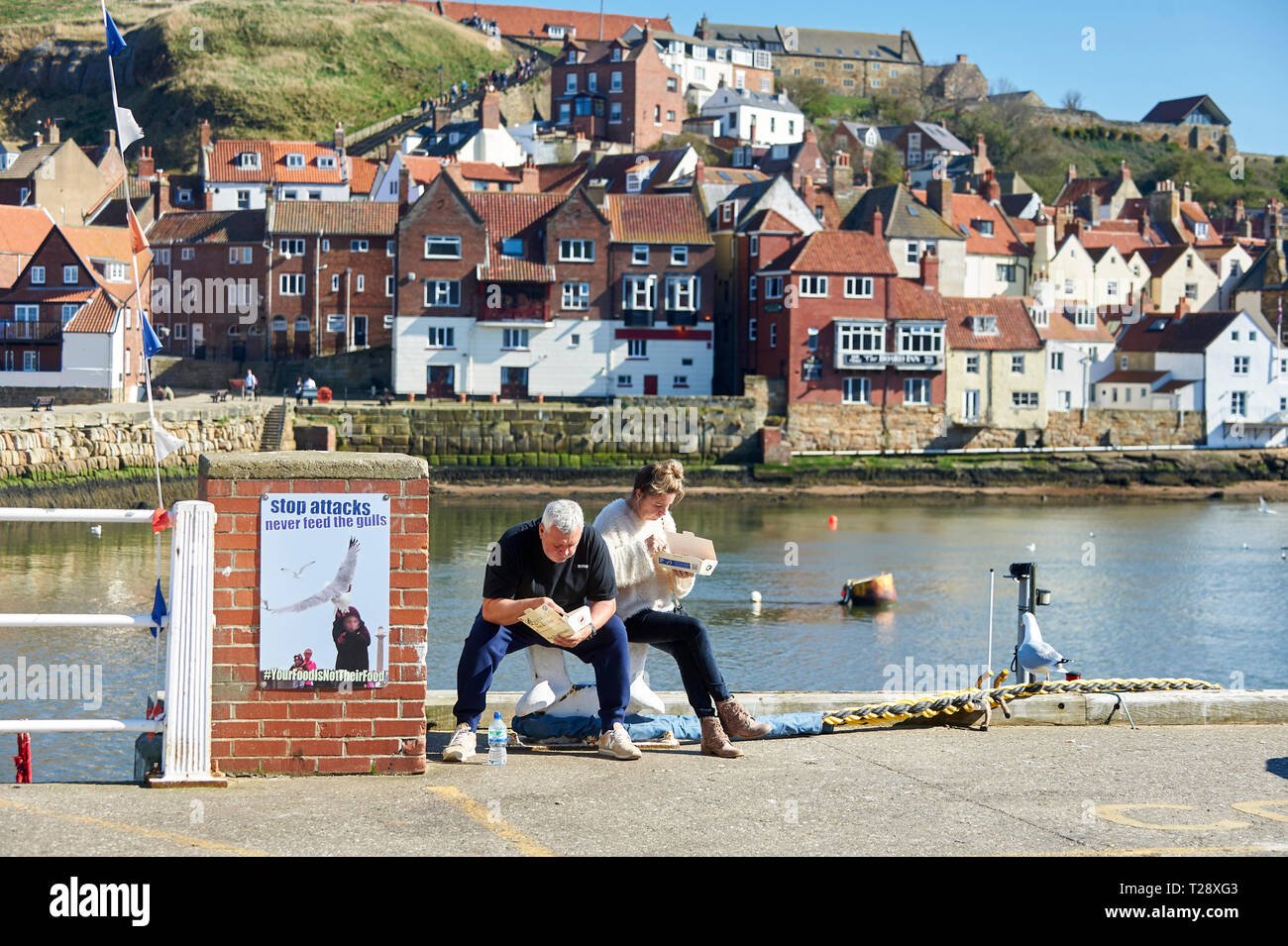 Couple eating Fish & Chips sitting on the harbour at Whitby , North ...