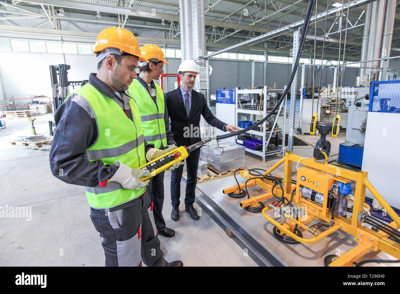 Manager and workers working with metal sheet lifting device at CNC ...