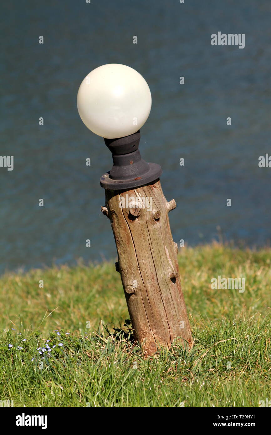 Round white backyard outdoor lamp mounted on tree stump leaning to one ...