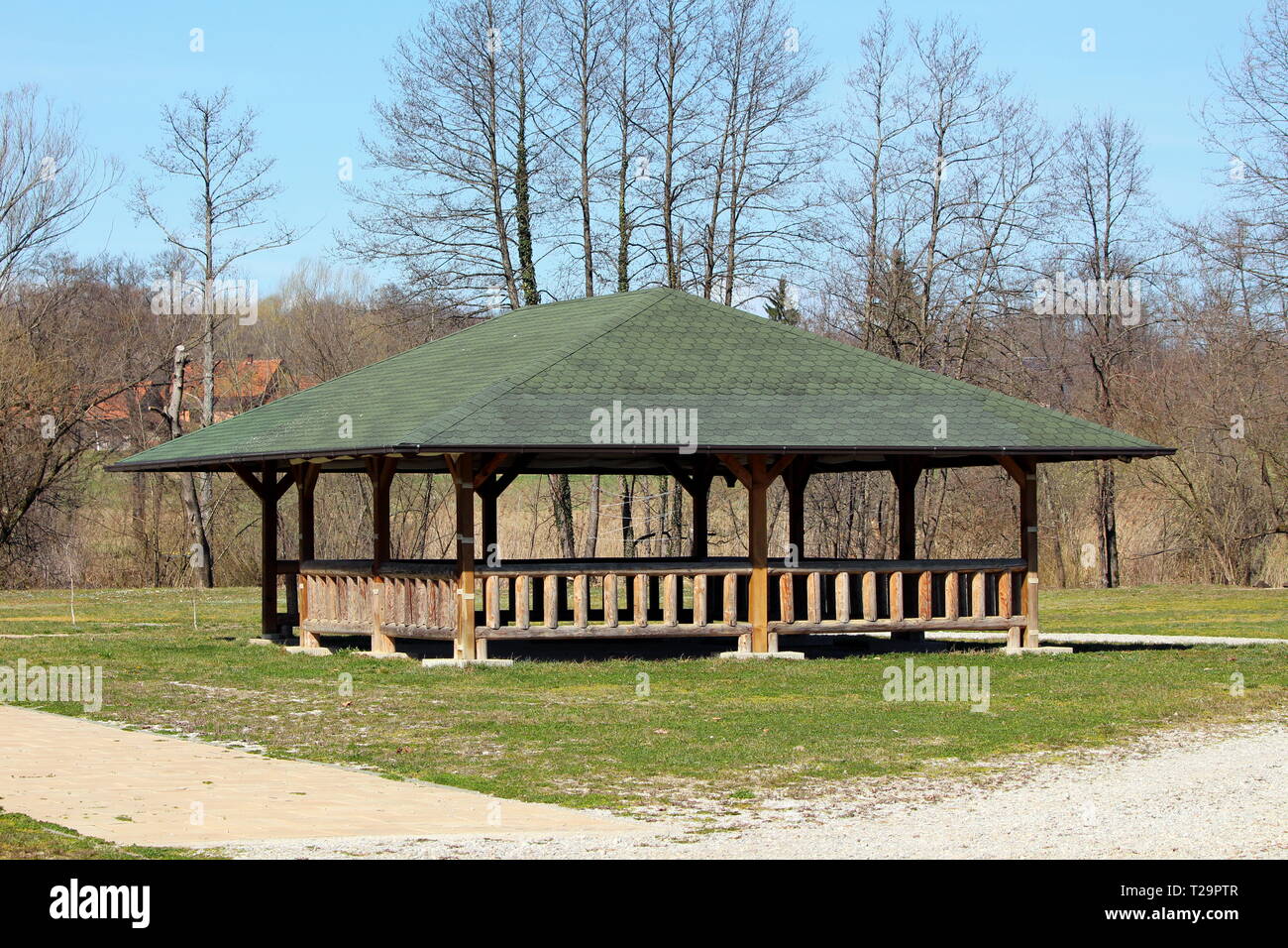 Wooden park pavilion with green roof tiles surrounded with grass and ...