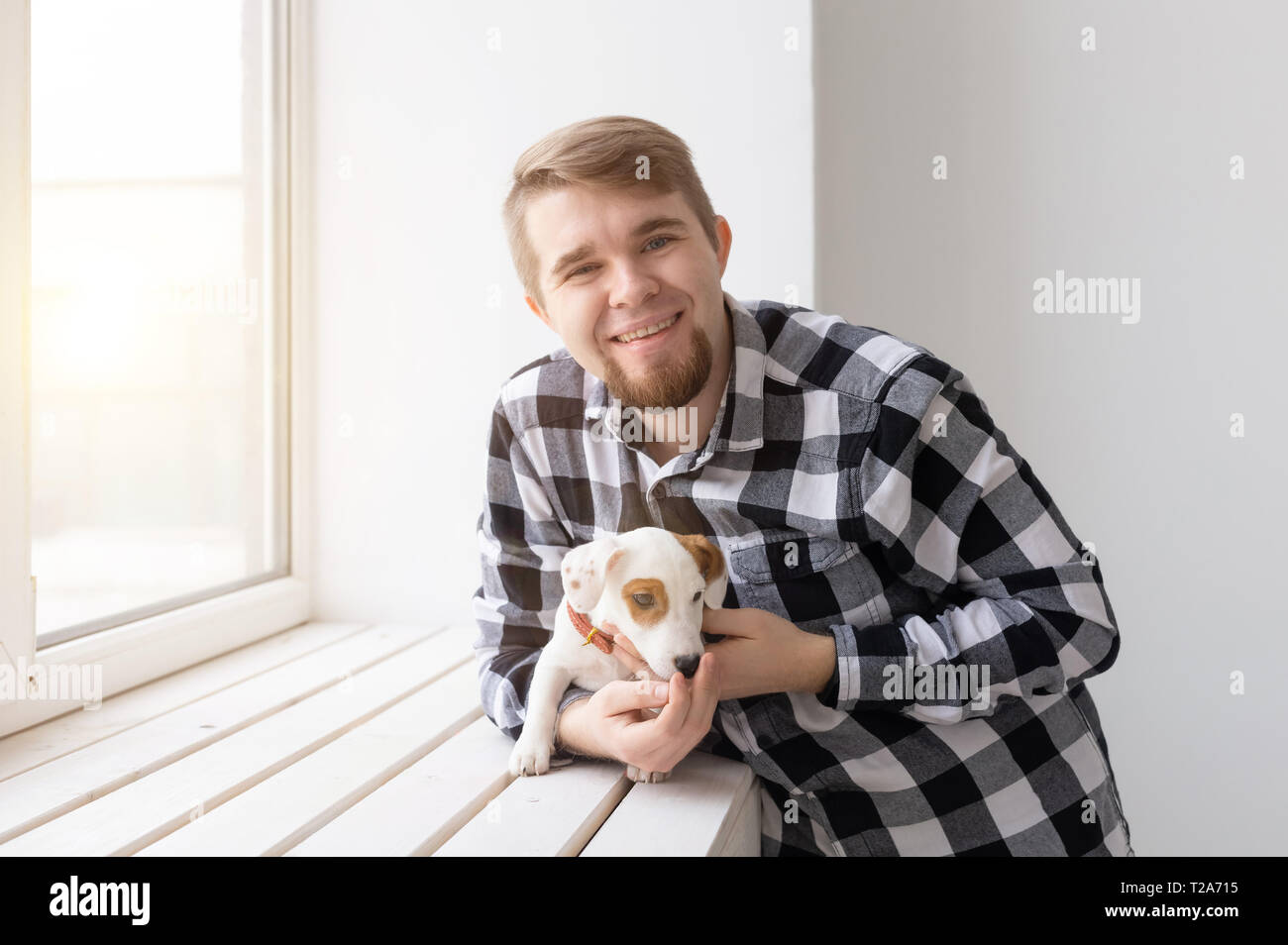people, pets and animals concept - young man hugging puppy near window ...
