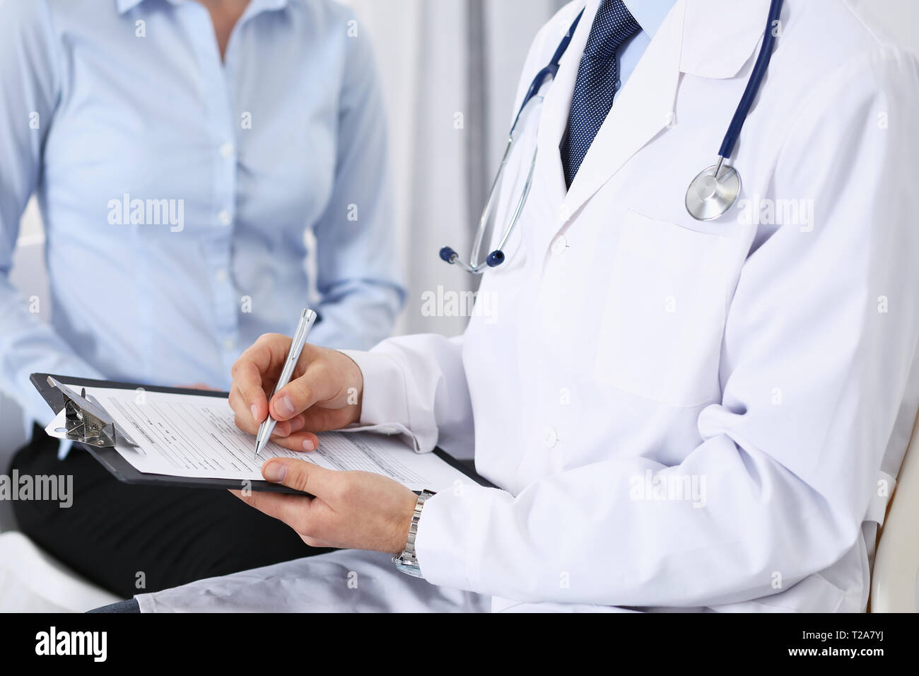 Male doctor holding application form while consulting female patient in ...