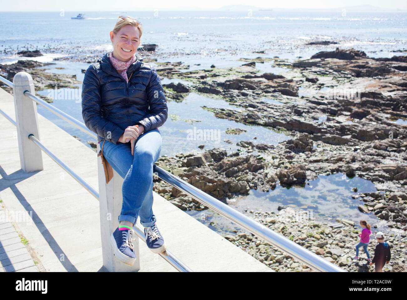 Woman sitting on railing along Sea Point Promenade, Cape Town Stock ...