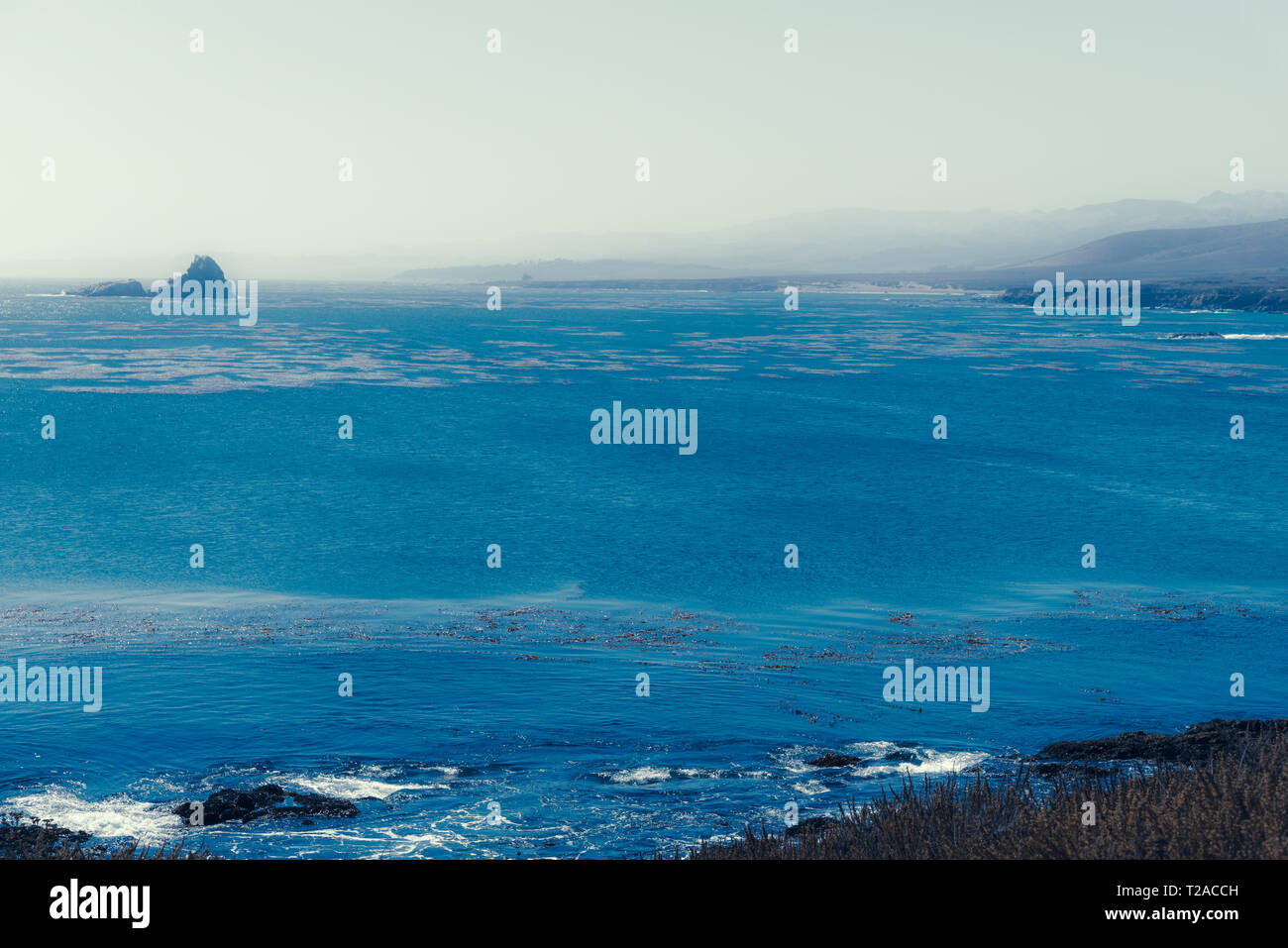 Overlooking blue ocean with white waves breaking onto rocks below ...