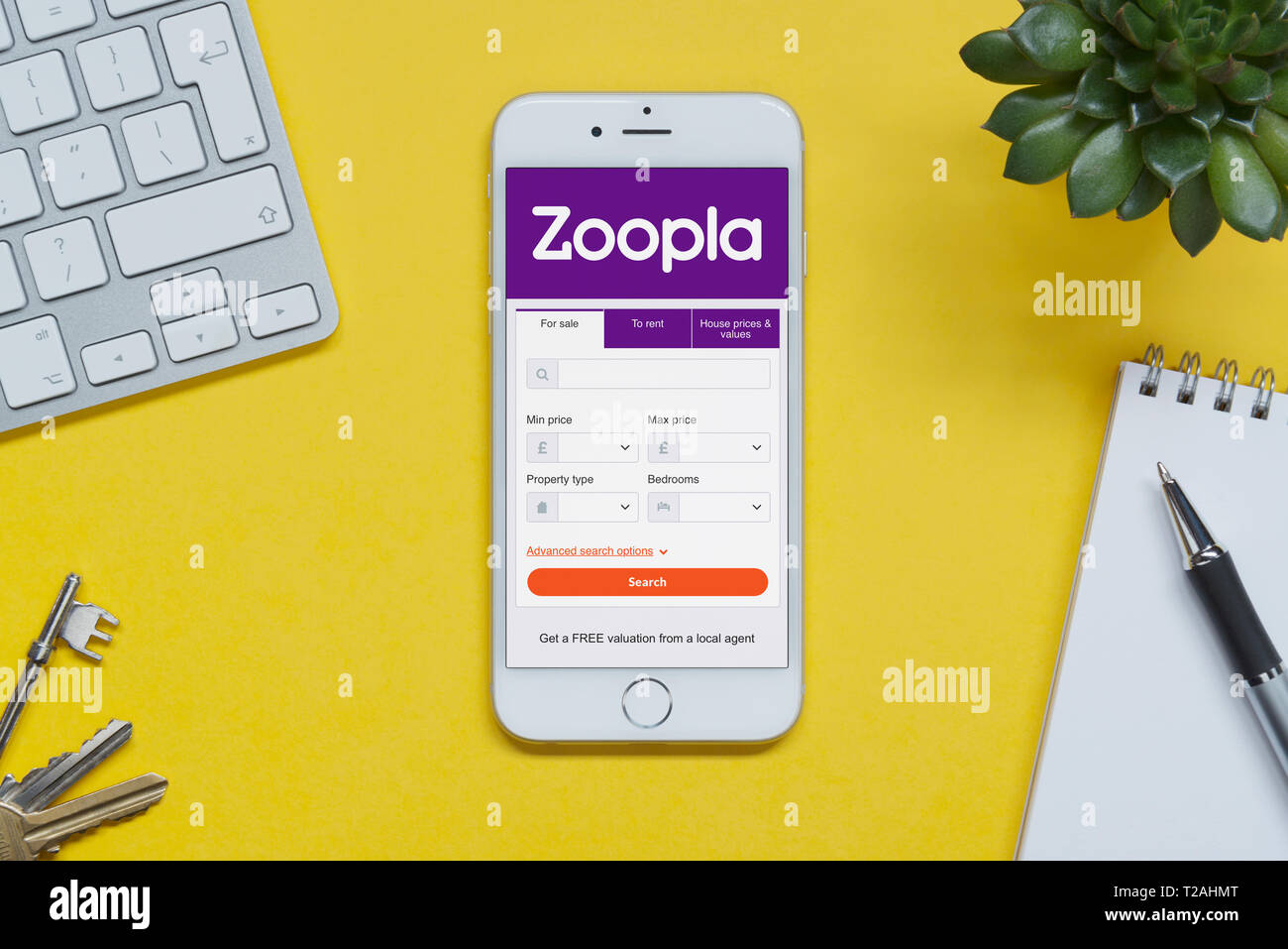 An iPhone showing the Zoopla website rests on a yellow background table ...