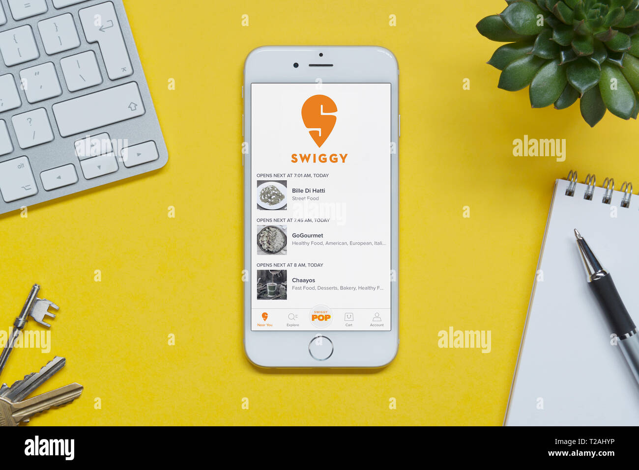 An iPhone showing the Swiggy website rests on a yellow background table ...