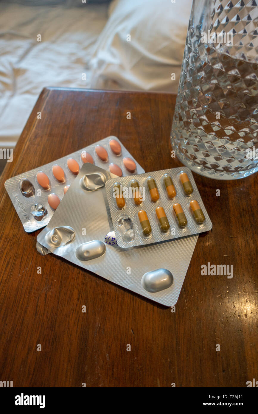3 packets of Prescription drugs and a glass of water on a bedside table ...