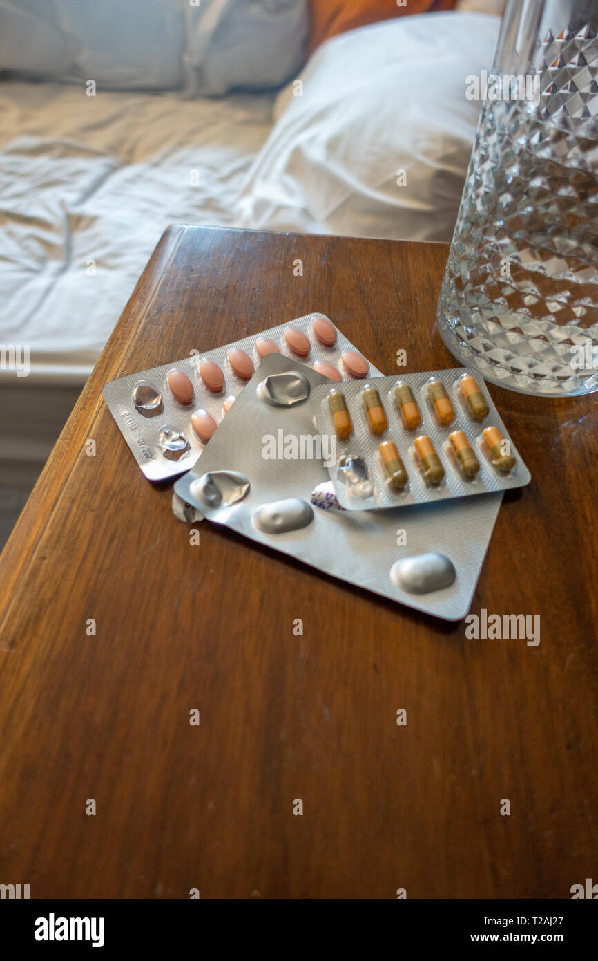 3 packets of Prescription drugs and a glass of water on a bedside table ...