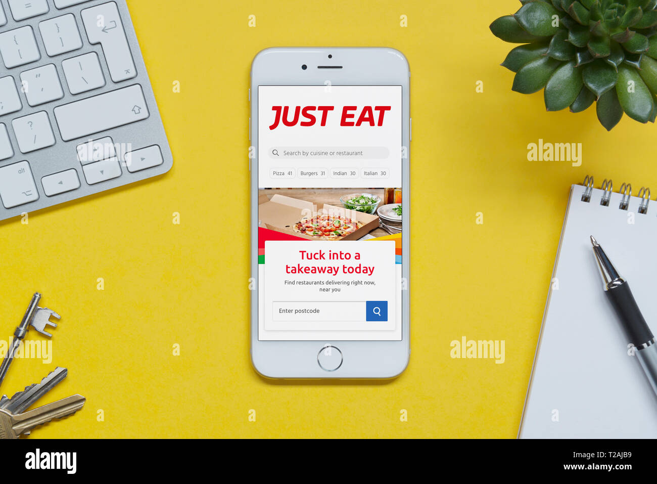 An iPhone showing the Just Eat website rests on a yellow background ...