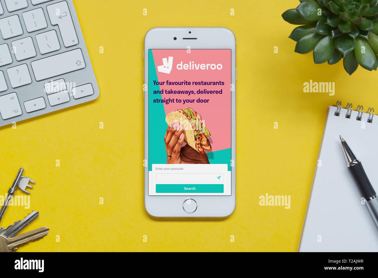 An iPhone showing the Deliveroo website rests on a yellow background ...