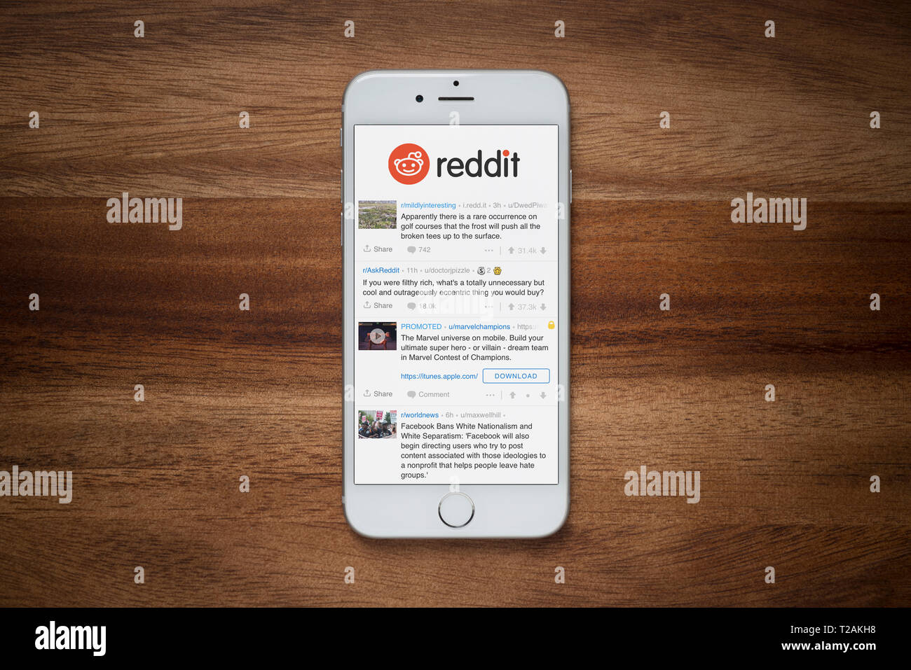 An iPhone showing the Reddit website rests on a plain wooden table ...