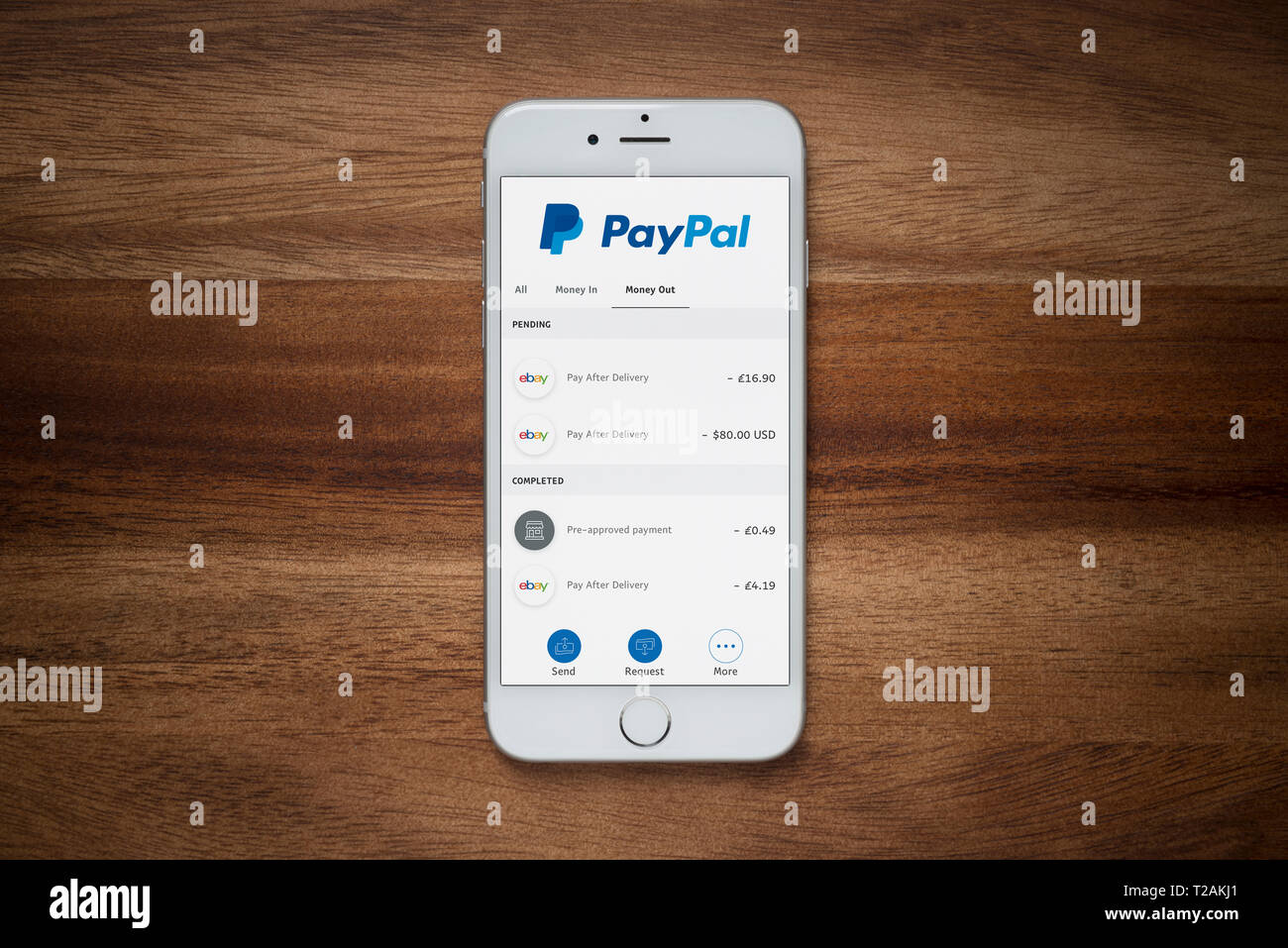 An iPhone showing the PayPal website rests on a plain wooden table ...