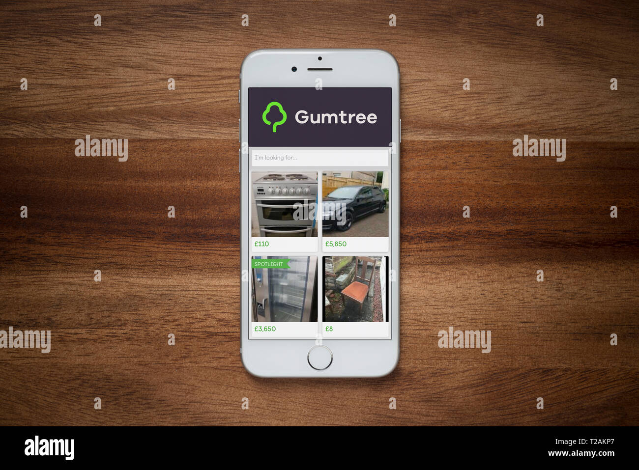 An iPhone showing the Gumtree website rests on a plain wooden table ...