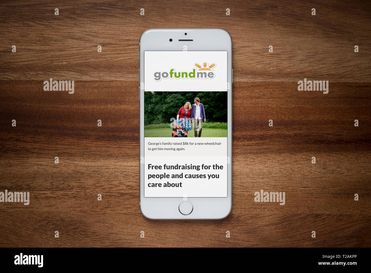 An iPhone showing the GoFundMe website rests on a plain wooden table ...