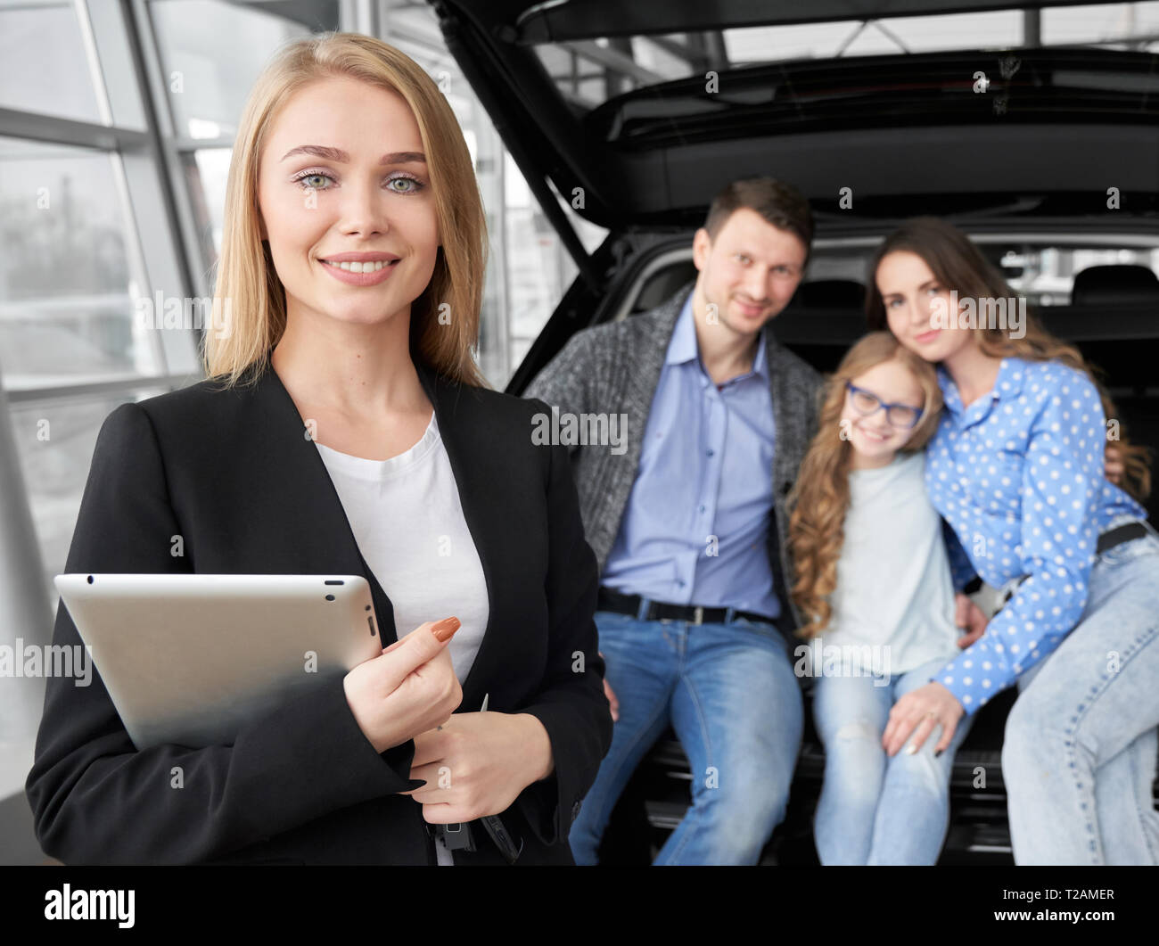 Front view of attractive car dealer in black suit keeping tablet ...