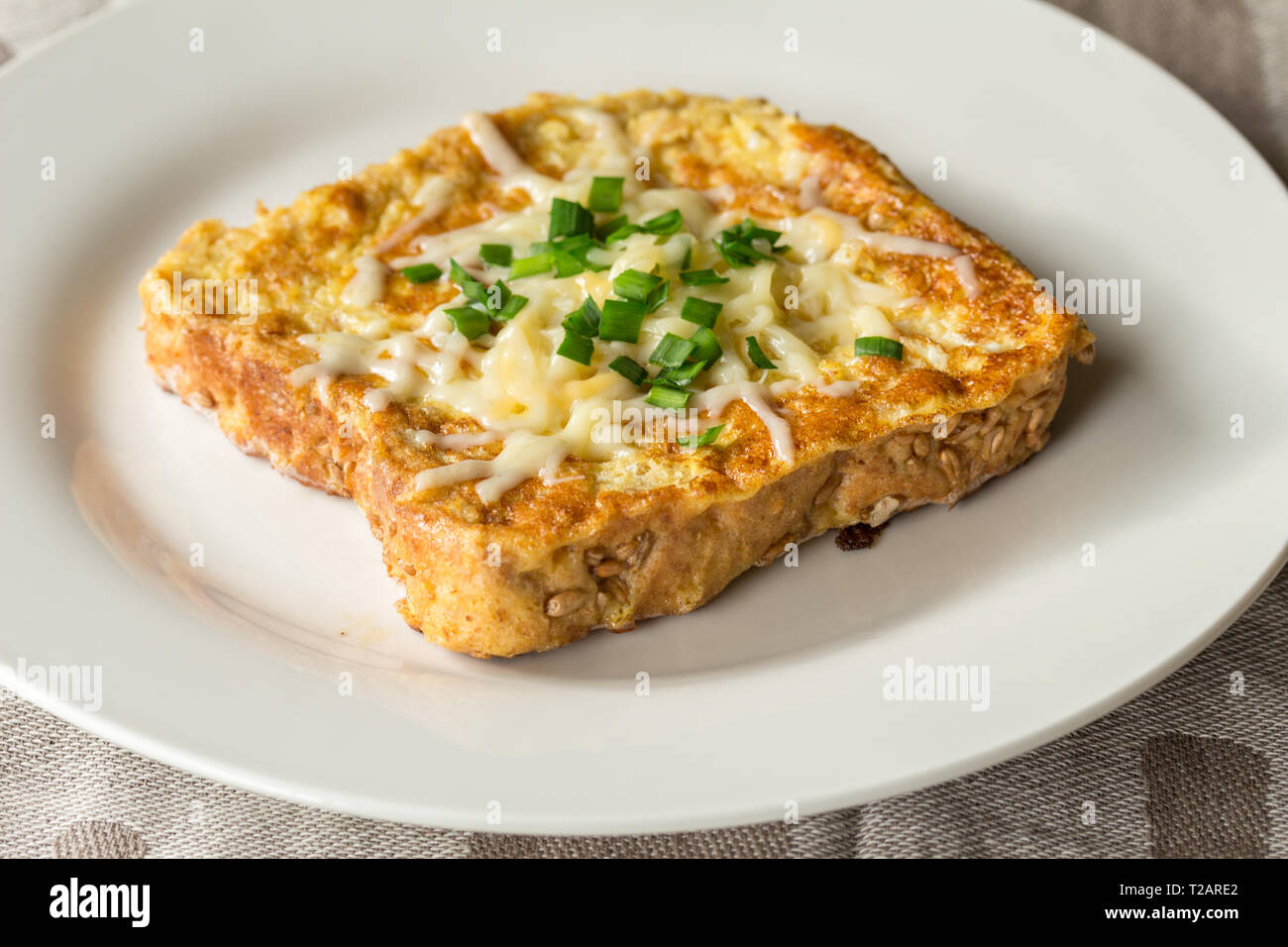 Savoury cheesy French toast slice with chives garnish close up on white ...