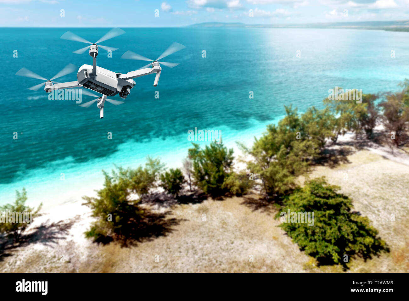 White drone with camera flying over the beach with green trees and blue ...