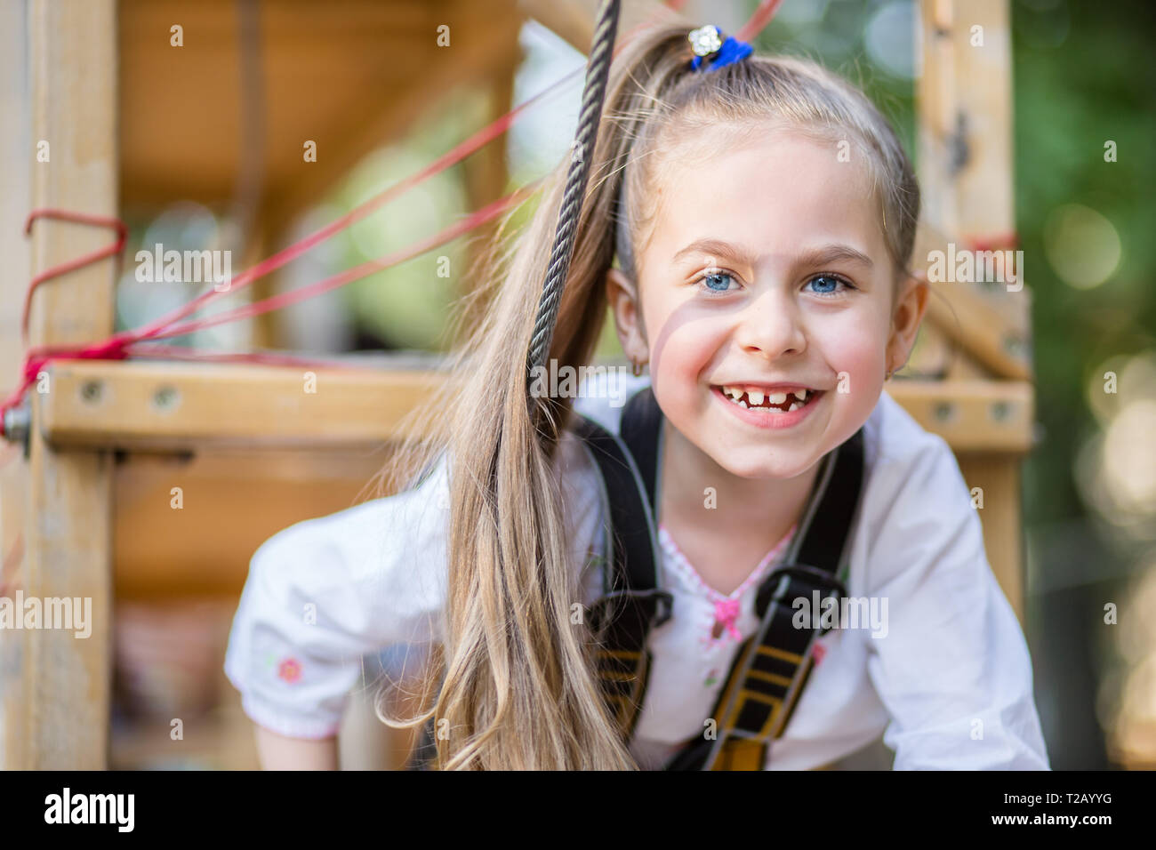 Portrait of a cute little girl who walks on a rope bridge in an ...