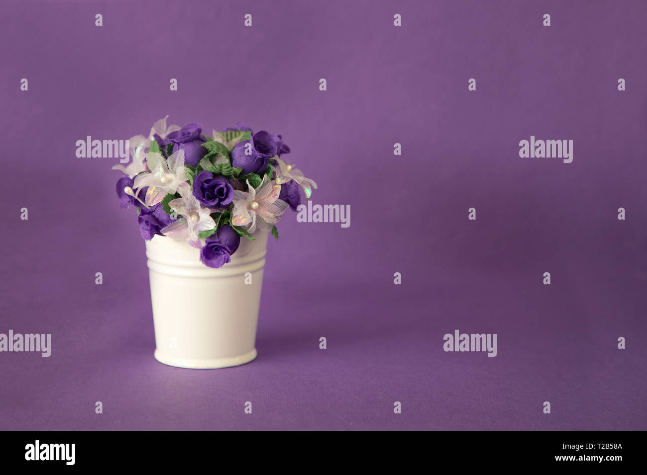 Pink and purple flowers in a white bucket on a purple background with ...