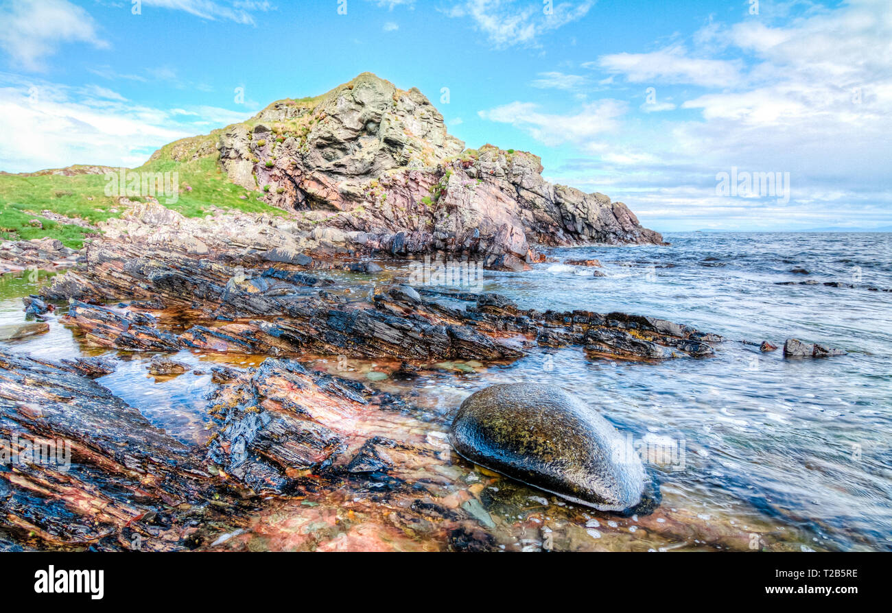 Jagged rock layers and boulders smoothed by the ocean are seen at an ...