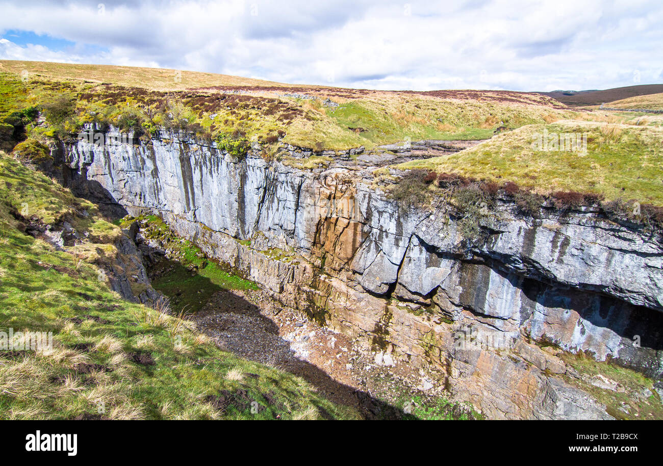 A large rock chasm with massive cliffs in a barren grassy landscape ...