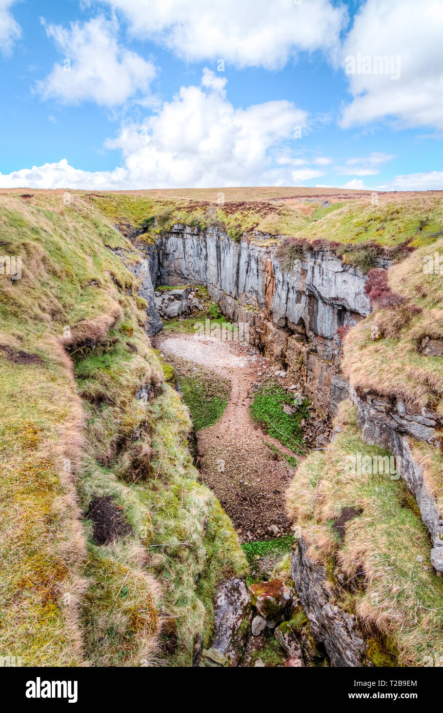 A large rock chasm with massive cliffs in a barren grassy landscape ...