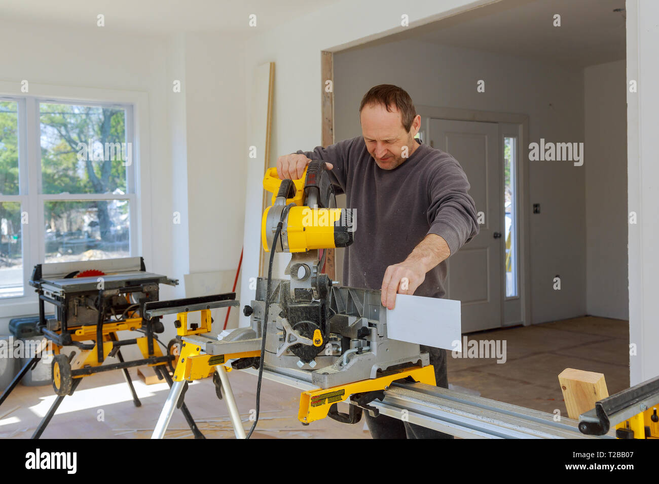 Carpenter using a circular saw to cut wood baseboard interior ...