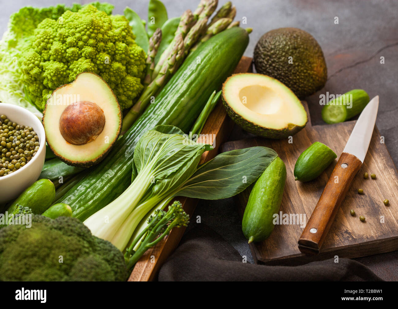 Assorted green toned raw organic vegetables in wooden box on dark stone ...