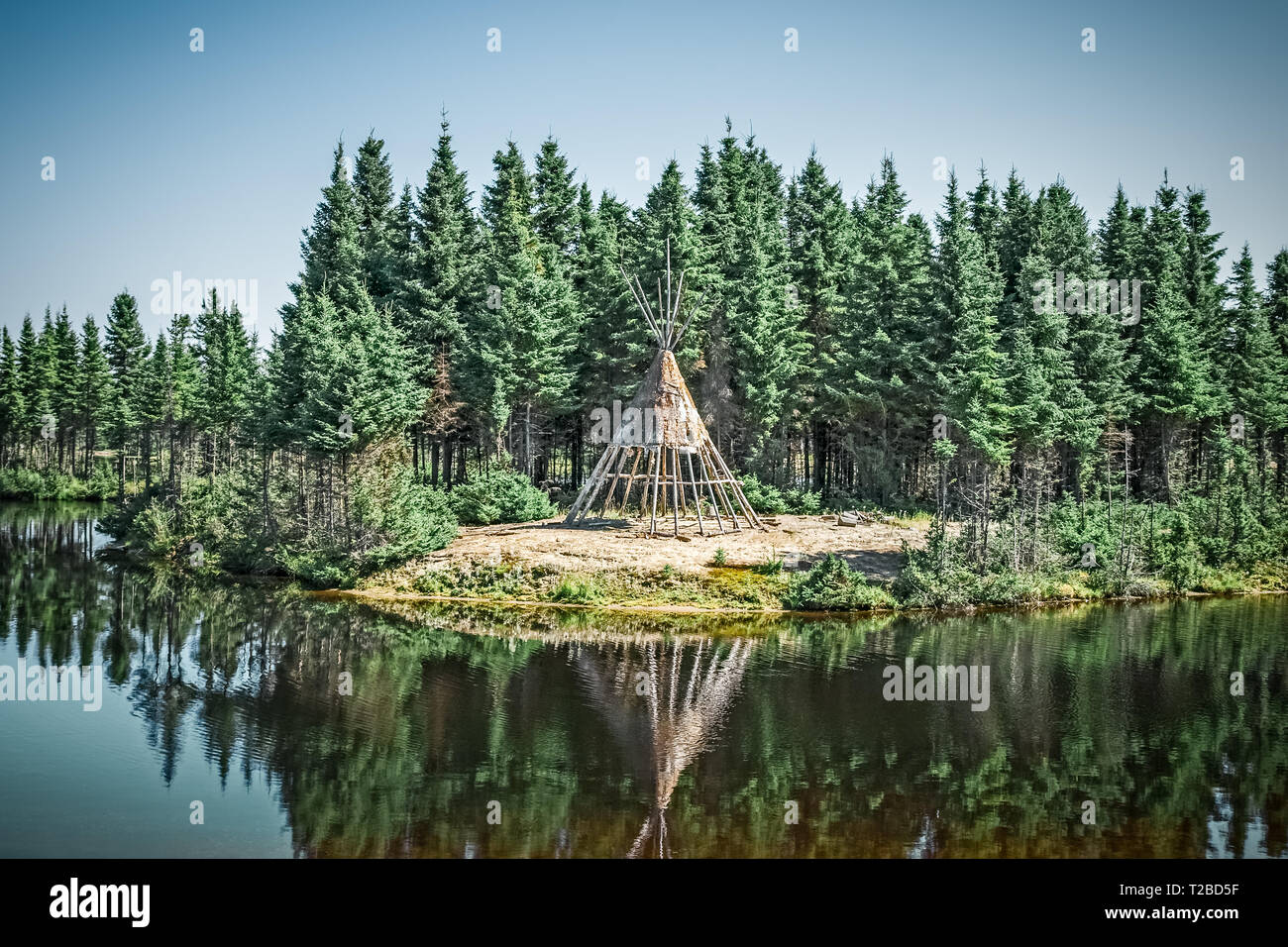 Traditional Native American tipi reflecting in the lake, surrounded by ...