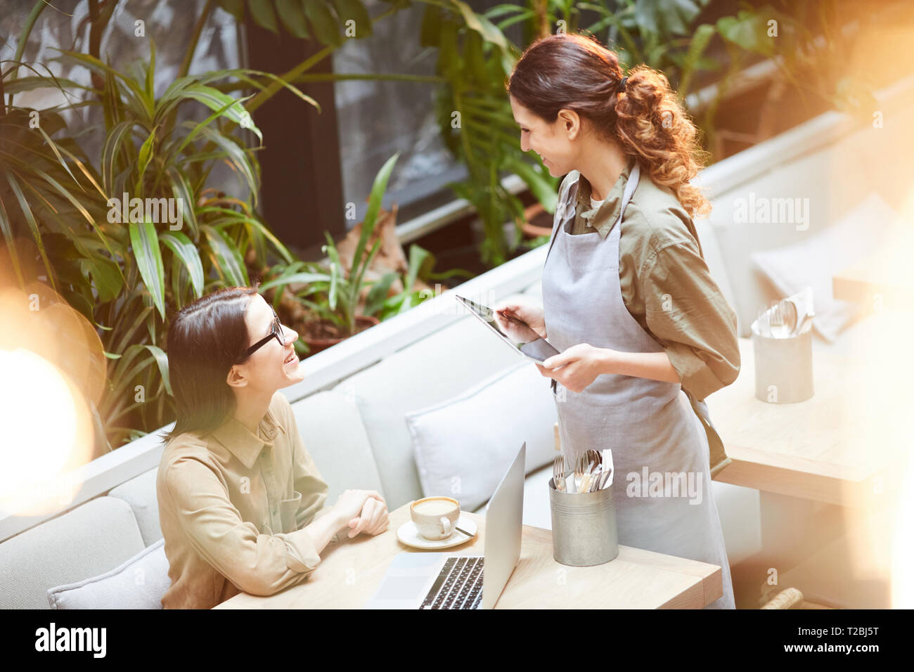 Waitress talking to young customer in cafe Stock Photo - Alamy