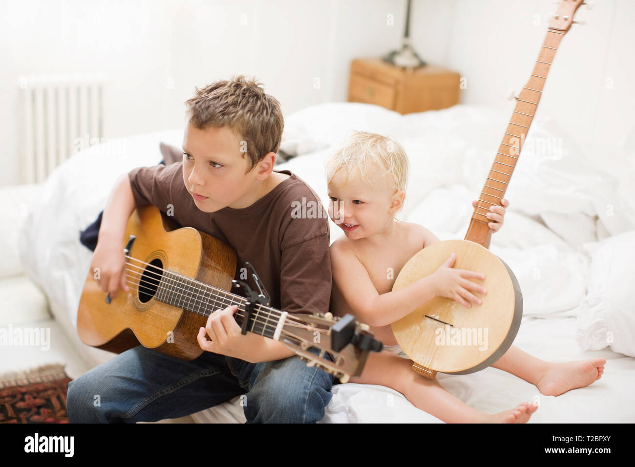 Boy playing a guitar while his toddler brother copies him with a banjo ...