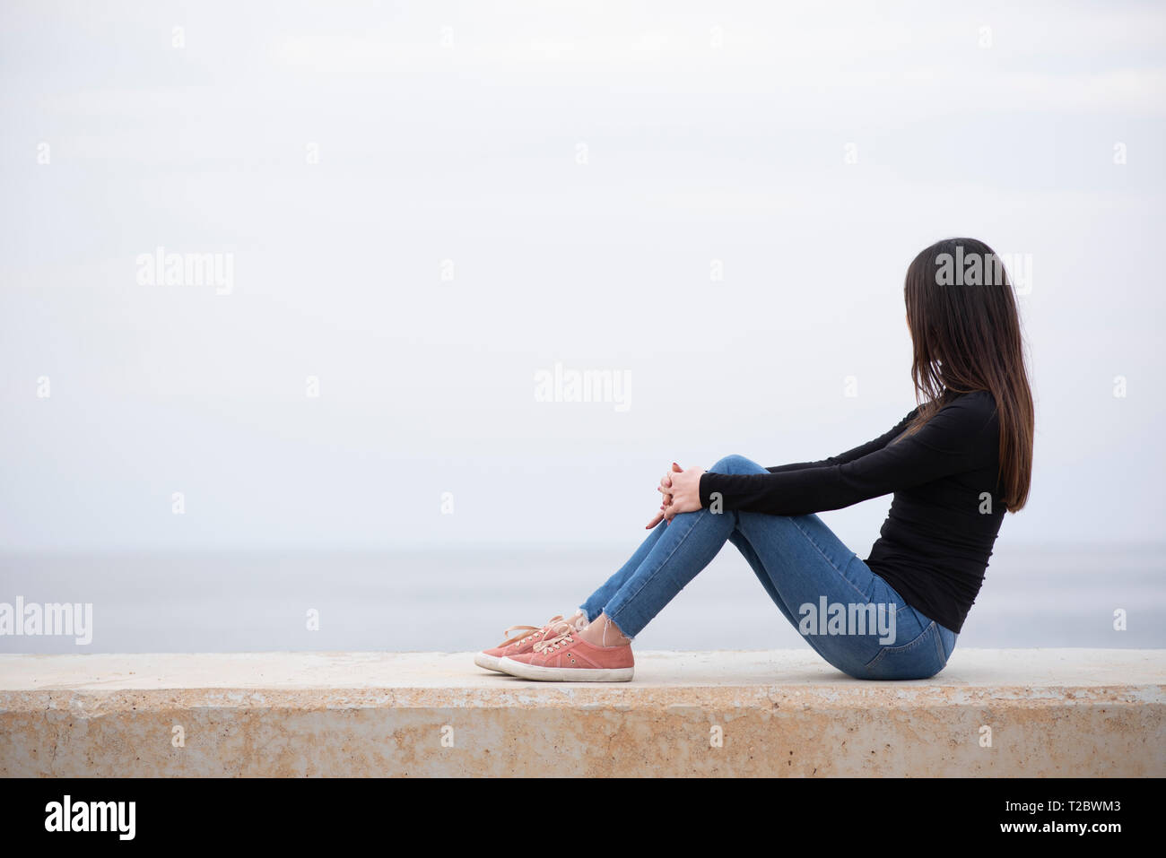 Side view of a young woman sat on the beach Stock Photo - Alamy