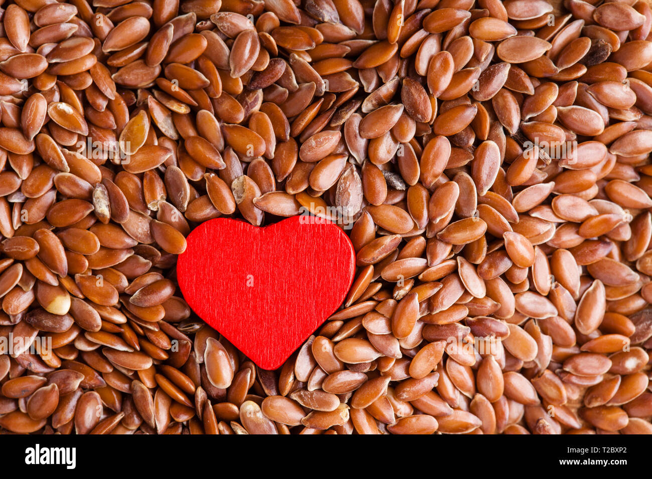 diet healthcare concept. Brown raw flax seeds linseed as natural background and red heart symbol ...