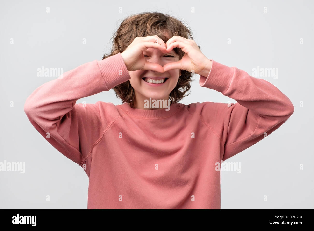 Smiling young woman making heart shape with fingers looking through eye ...