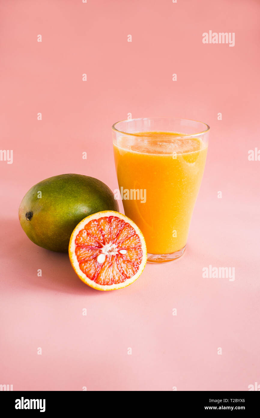 Glass of mango and orange juice on pink background. Refreshments and ...