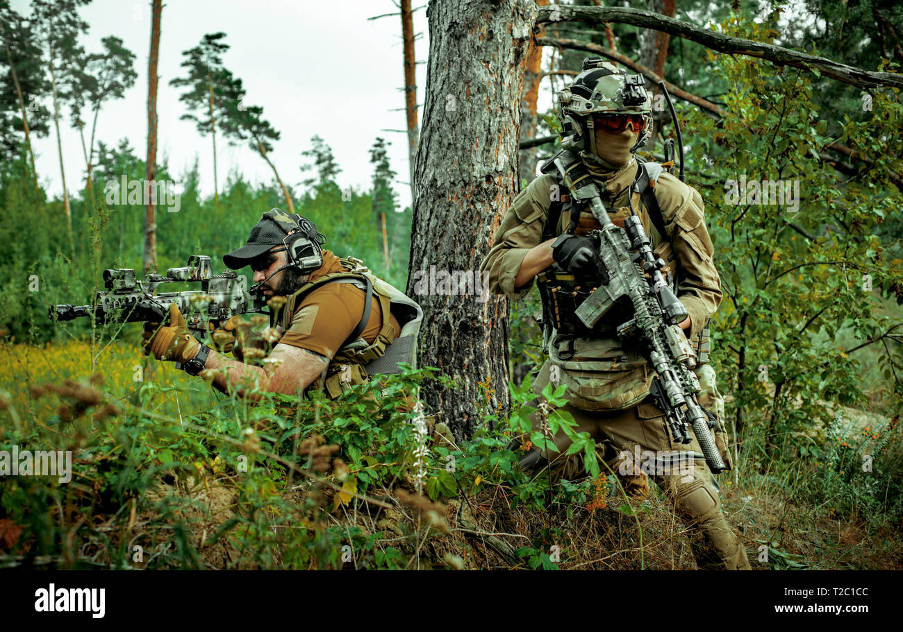 Airsoft men with guns stand back to back. Soldiers stand on hill and on ...