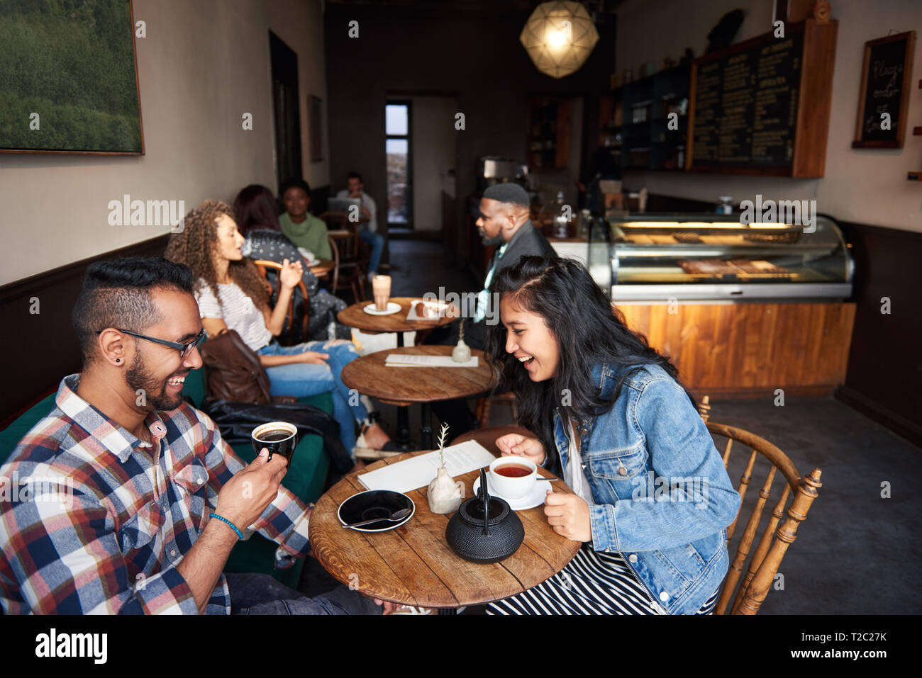 Diverse young people drinking coffee and talking while sitting together ...