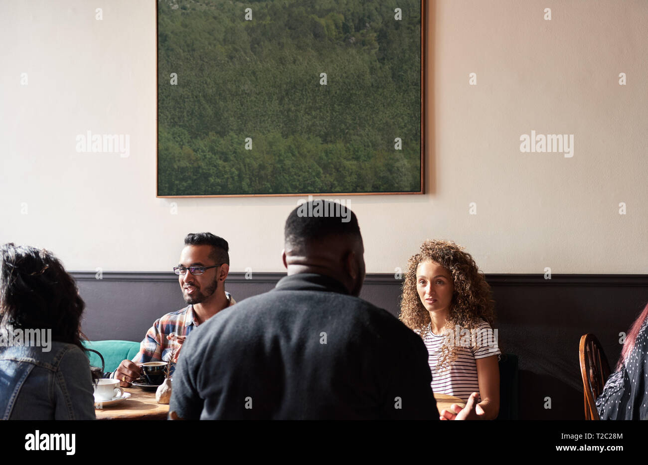 Group of diverse young people sitting together at tables in a trendy ...