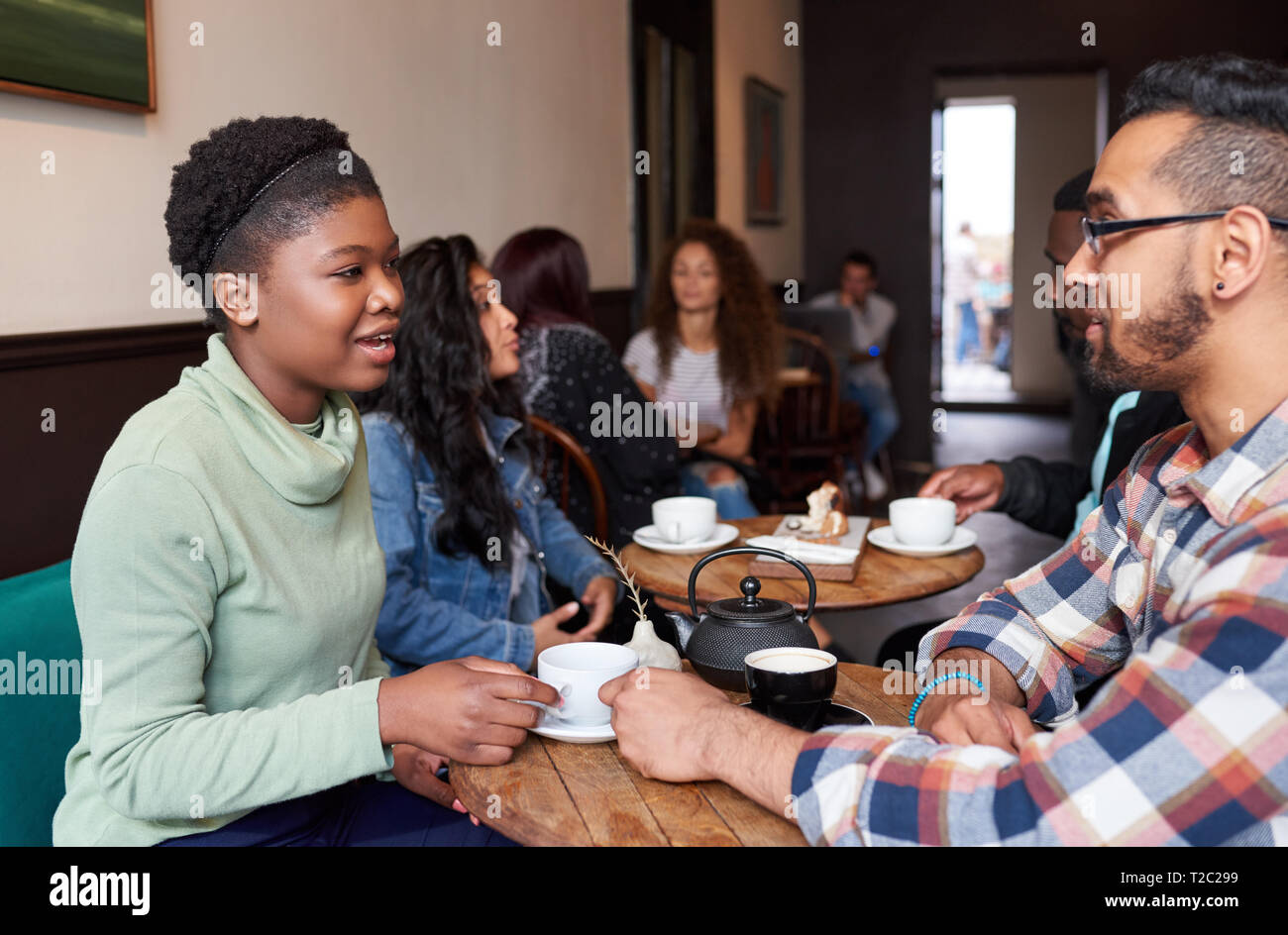 Two young friends talking together over coffee while sitting at a table ...