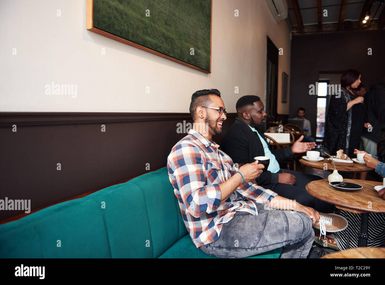 Two young men sitting at a table in a trendy cafe drinking coffee and ...