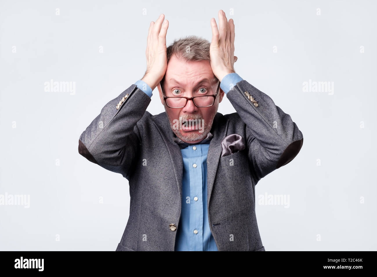 Shocked dazed senior man in suit holding head with both hands. He is in ...